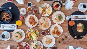 Diversos pratos e bebidas de café da manhã dispostos sobre uma mesa de madeira.