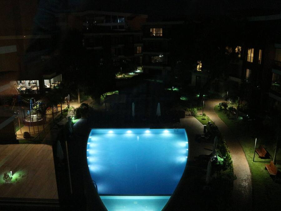 Vista noturna de um pátio de hotel com piscina, iluminado por luzes artificiais.