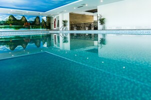 Uma grande piscina interior com superfície de água azul e límpida, rodeada por um deck ladrilhado.
