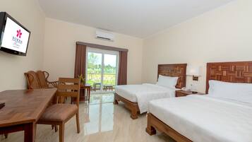 Quarto de hotel com duas camas, uma mesa de jantar de madeira, cadeiras, televisão e vista para o exterior.