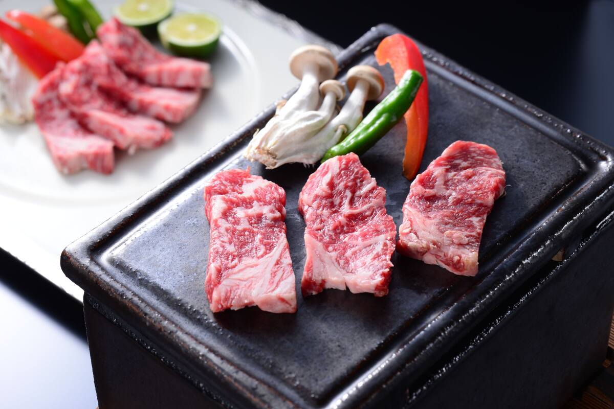 Uma grelha preta com carne crua e legumes.