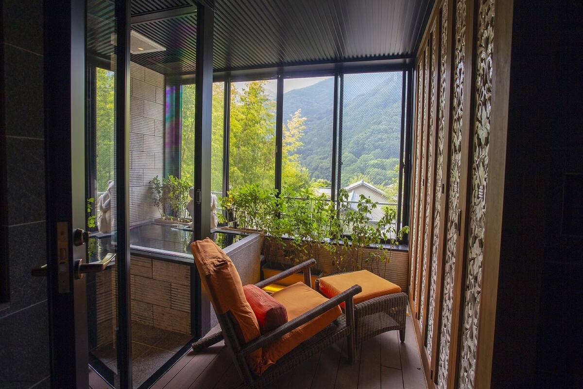 Quarto com vista para uma montanha, uma cadeira com almofadas e uma porta de vidro que dá para o exterior.