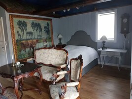 Quarto com cama, escrivaninha, duas cadeiras, um quadro e um relógio.