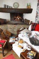 Uma sala de estar aconchegante com lareira, um sofá com almofadas florais, uma mesa de jantar com itens de café da manhã e uma estante de livros.