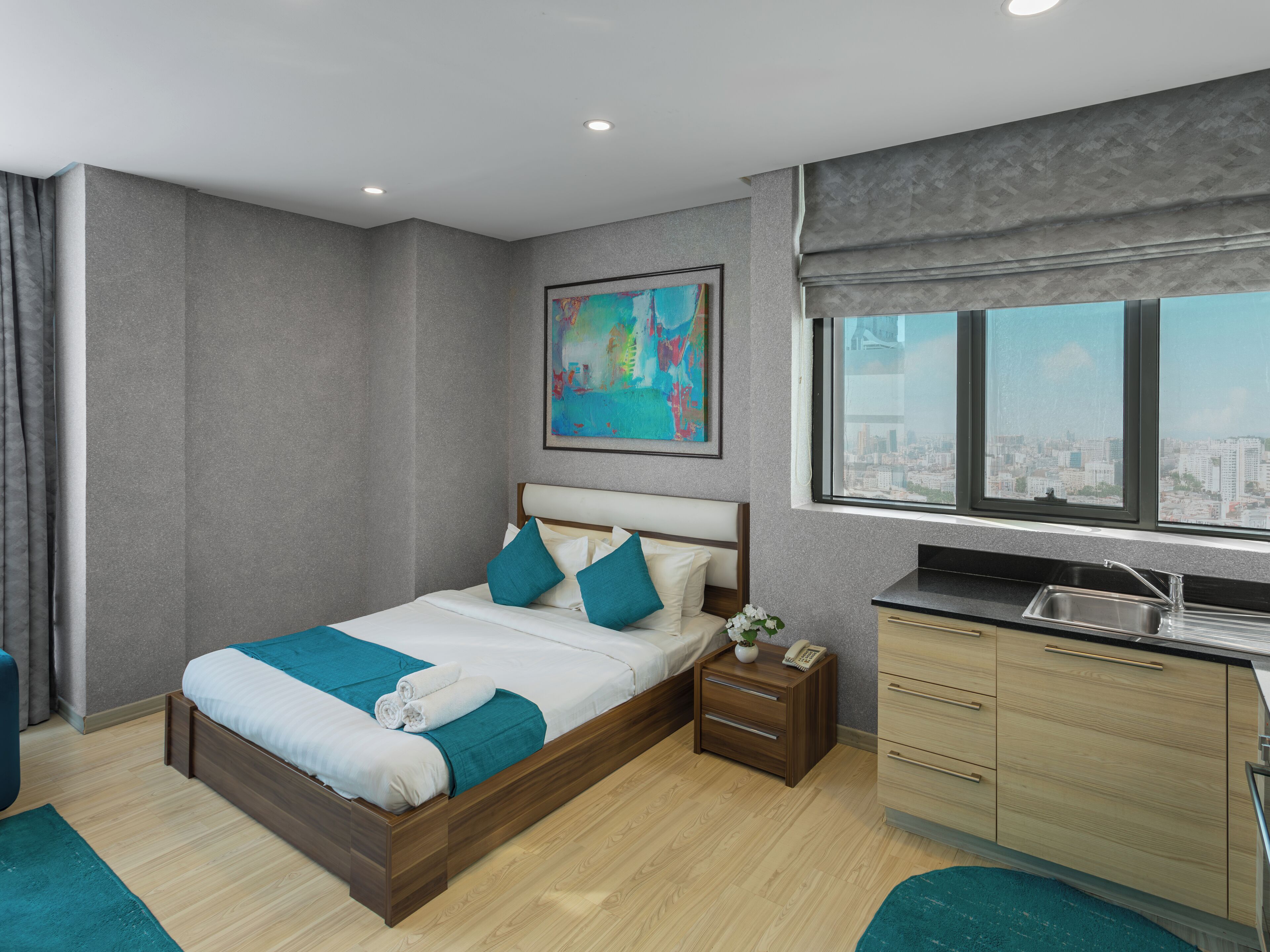 Quarto de hotel moderno com cama, mesa de cabeceira, escrivaninha e janela com vista para a cidade.