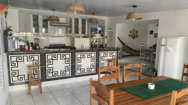 Cozinha moderna com ilha central, armários brancos e área de jantar com cadeiras de madeira e um jogo americano verde.