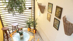 Um pequeno pátio com uma mesa de vidro redonda, cadeiras amarelas e plantas em vasos.