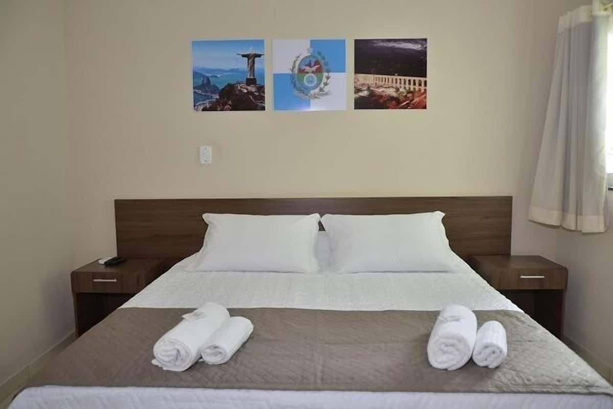 Quarto de hotel com uma cama grande, duas mesas de cabeceira e três quadros na parede.