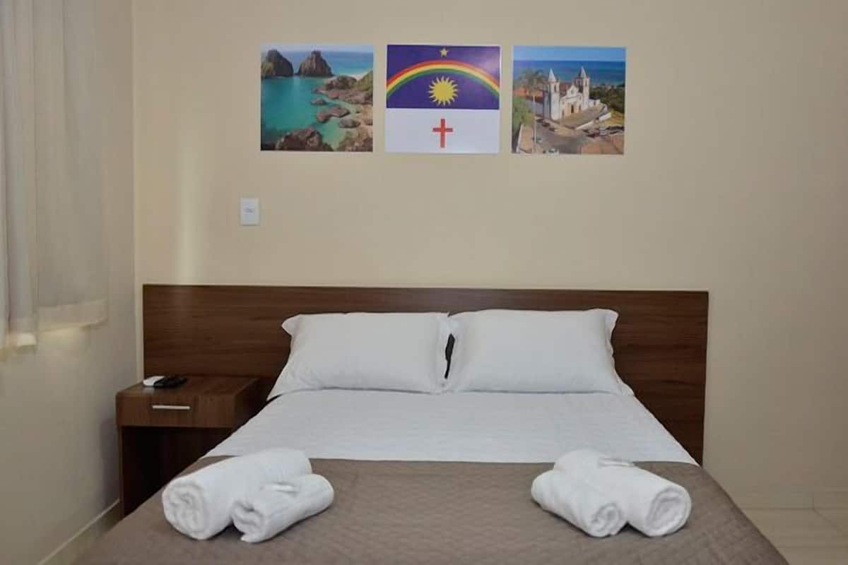 Cama bem arrumada com lençóis e toalhas brancas, cabeceira de madeira e mesa de cabeceira com telefone.