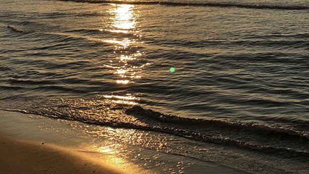 Uma praia ao pôr do sol, com o sol refletindo na água.