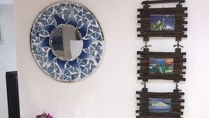 Uma mesa de madeira com uma orquídea em vaso, um espelho decorativo e um porta-retrato de madeira com fotografias em uma parede branca.
