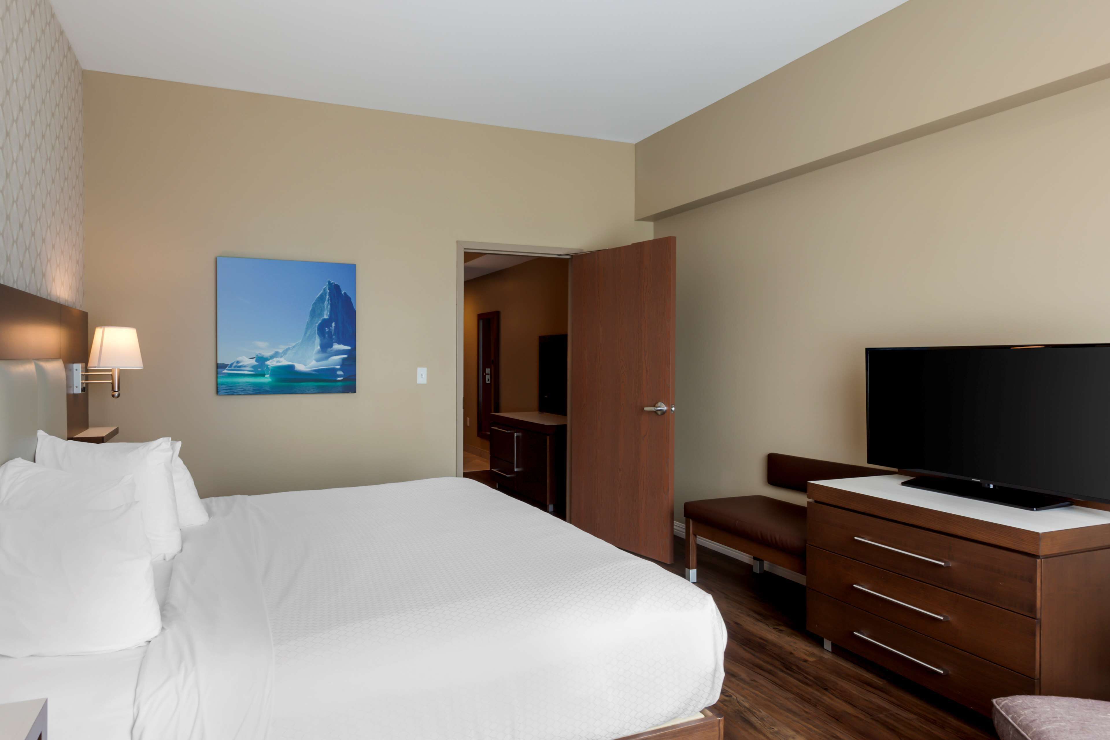 Quarto de hotel com uma cama grande, televisão, cómoda de madeira e um quadro na parede.