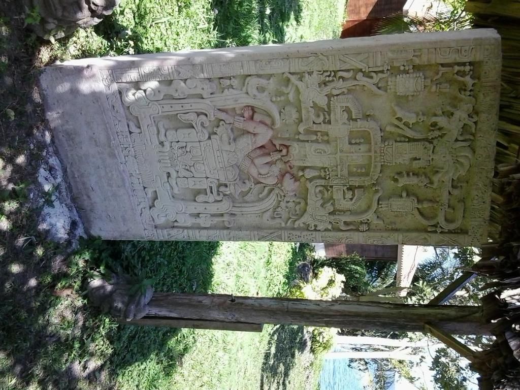 Monumento de pedra com esculturas detalhadas, possivelmente com significado histórico ou cultural, situado em um ambiente natural ao ar livre.