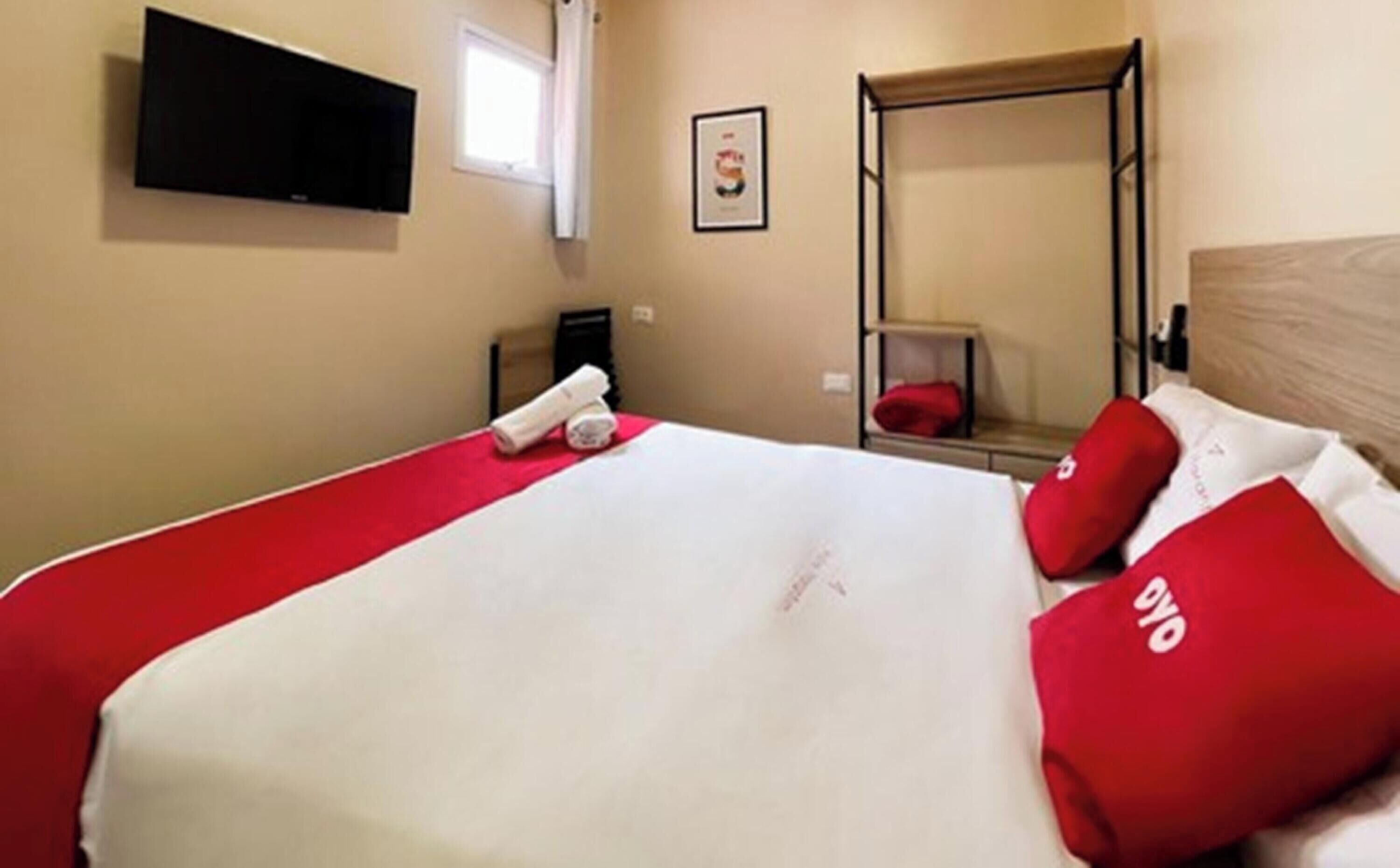 Quarto de hotel com cama, TV fixada na parede, janela e quadro na parede.