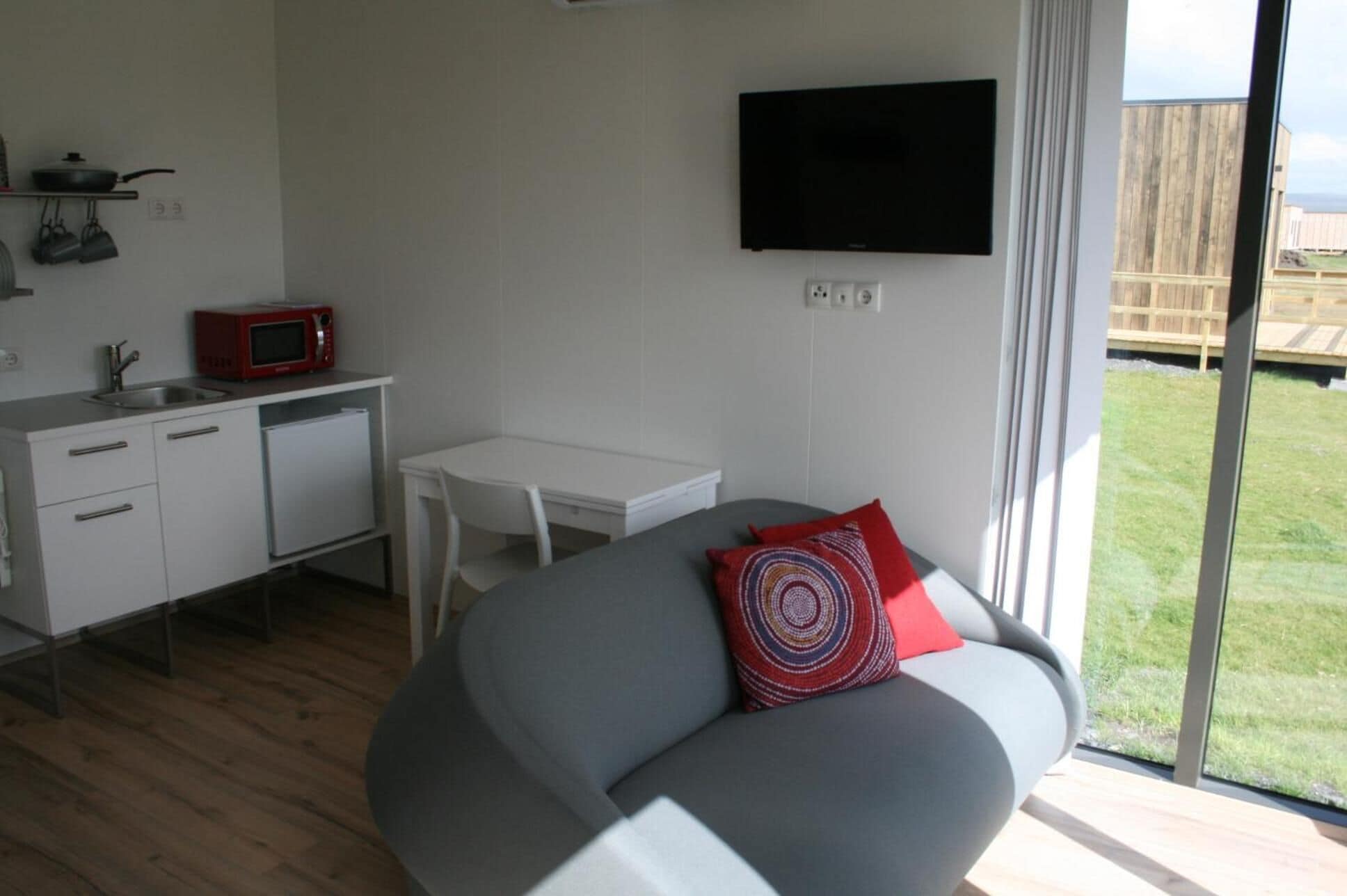 Um espaço de estar moderno com sofá, televisão de tela plana, cozinha compacta com micro-ondas e mesa de jantar.