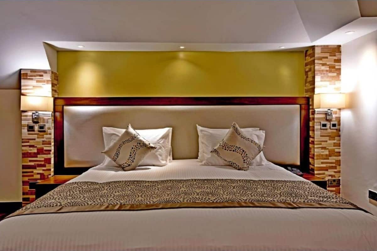Quarto de hotel com cama grande, duas luminárias de cabeceira, cabeceira com padrão geométrico e manta decorativa.