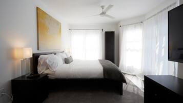 Quarto moderno com cama, mesas de cabeceira, ventilador de teto e uma janela grande com cortinas.