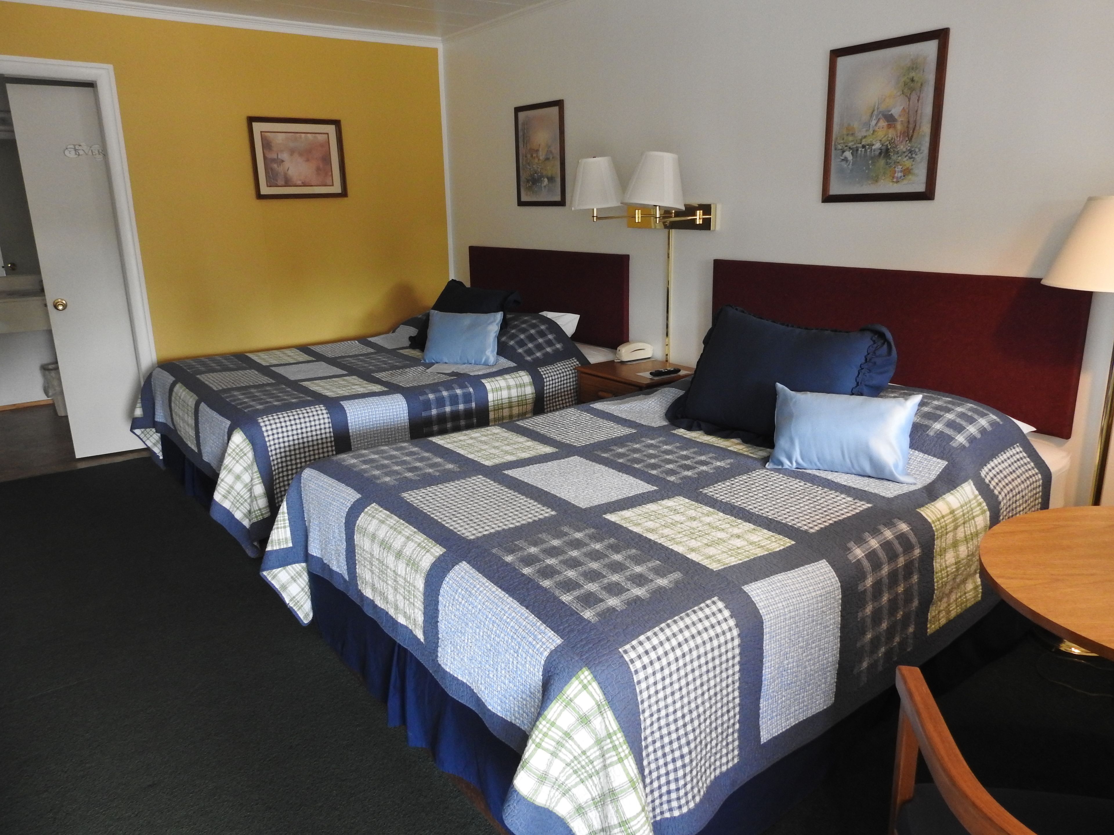 Quarto de hotel com duas camas, uma escrivaninha, uma cadeira e uma mesinha.