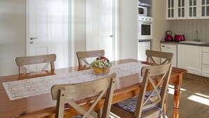 Uma área de refeições com uma mesa de madeira, quatro cadeiras, uma fruteira e um jogo americano de renda branca.
