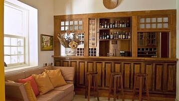 Uma área de bar com armários de madeira, um sofá com almofadas e um vaso com flores secas.