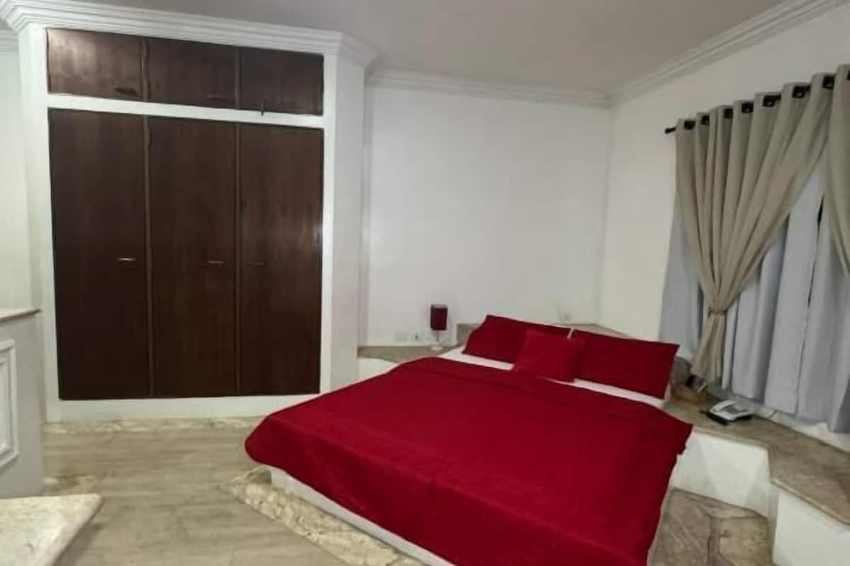 Quarto com cama, guarda-roupa, mesa de cabeceira e janela com cortinas.