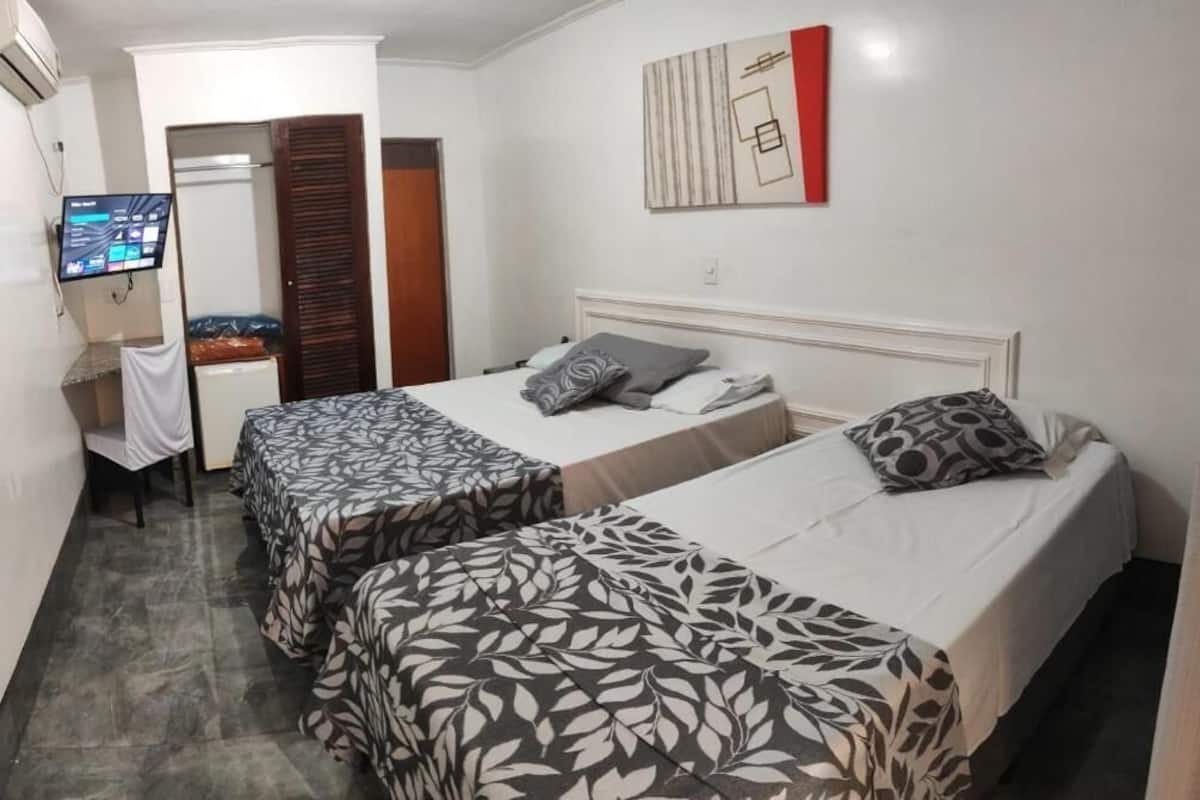 Quarto de hotel com duas camas, uma televisão e um guarda-roupa.