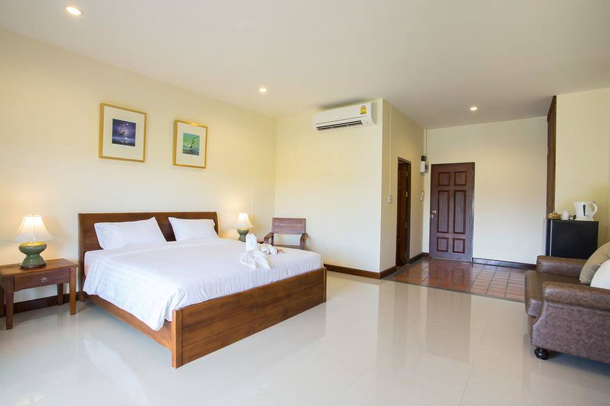 Quarto de hotel com cama de madeira, duas mesas de cabeceira com luminárias, uma TV de tela plana e uma porta que dá para outro quarto.