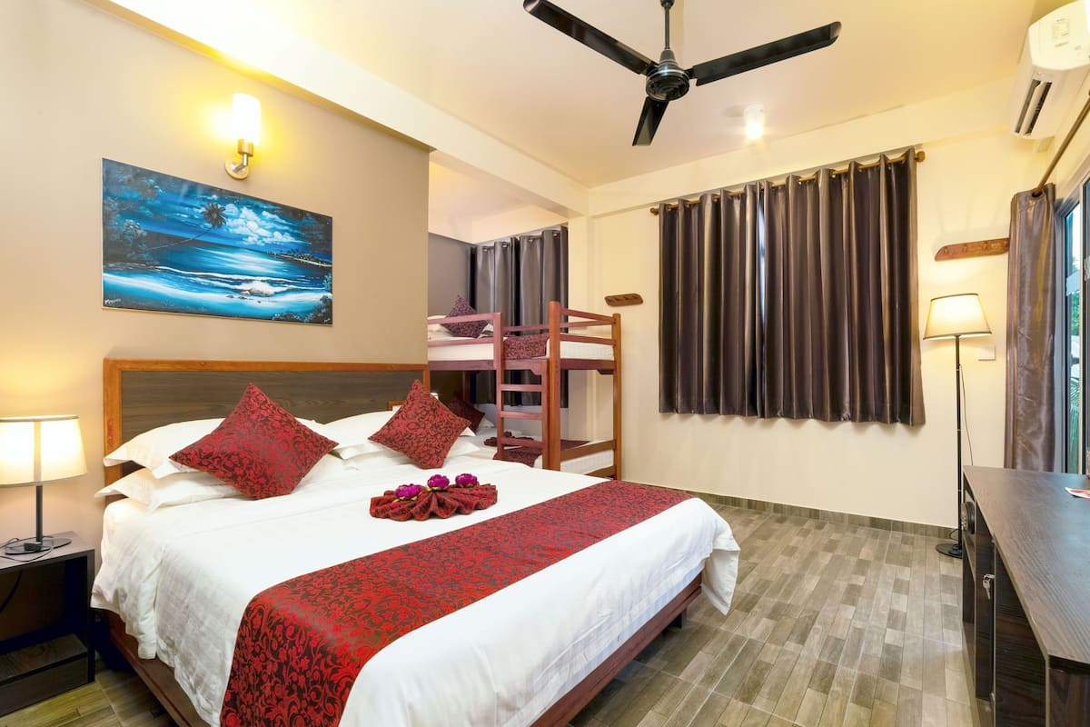 Quarto de hotel com cama, beliches, ventilador de teto, ar condicionado, um quadro e uma janela com cortinas.