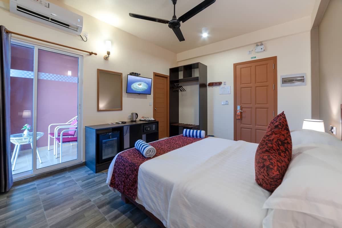 Quarto de hotel com cama, escrivaninha, televisão e porta de correr para uma varanda.