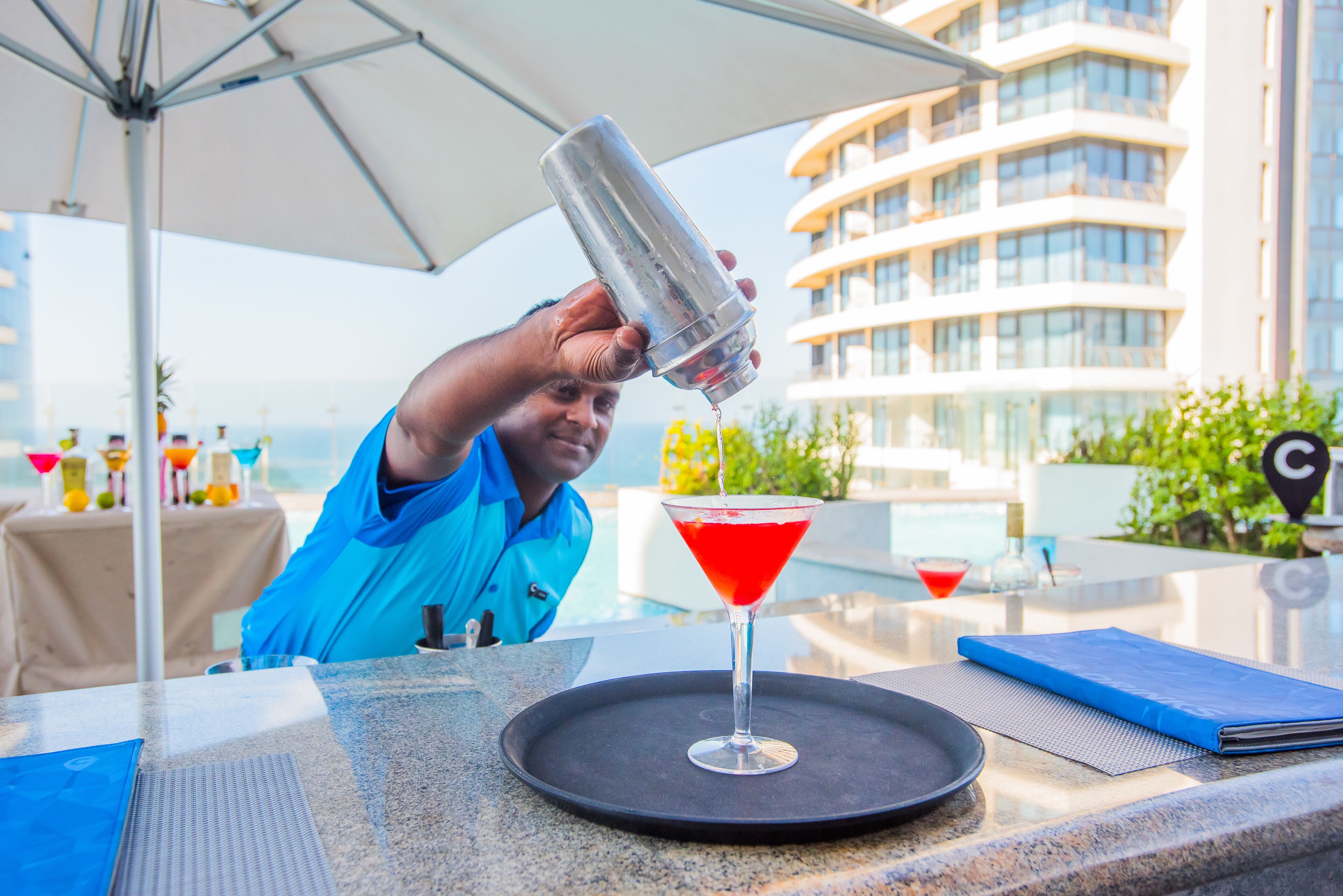 Um cocktail a ser servido em taça de martini sobre uma mesa, com um edifício moderno ao fundo.