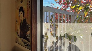 Quarto com um cartaz tradicional japonês na parede, janela com vista para uma árvore e um edifício lá fora.