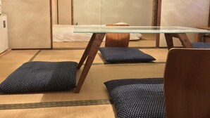Quarto com piso de tatame, mesa com tampo de vidro e cama com roupa de cama branca.