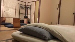 Um quarto tradicional japonês com tatames, uma mesa de madeira baixa e uma cama com travesseiros.