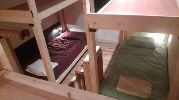 Quarto com beliche de estrutura de madeira, uma cama de solteiro com colchão verde e uma cama inferior com colchão roxo.