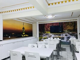 Um restaurante com mesas e cadeiras brancas, um grande mural de uma paisagem urbana ao pôr do sol e uma cena de cachoeira na parede.