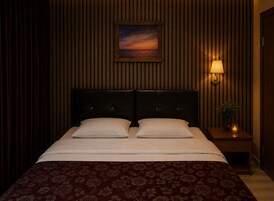 Quarto de hotel com cama, mesa de cabeceira com abajur, quadro na parede e janela com cortinas.