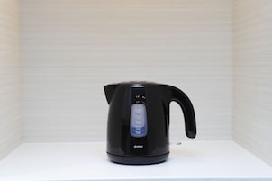 Uma chaleira elétrica preta com visor digital e alça, posicionada sobre uma superfície branca em frente a uma parede texturizada.