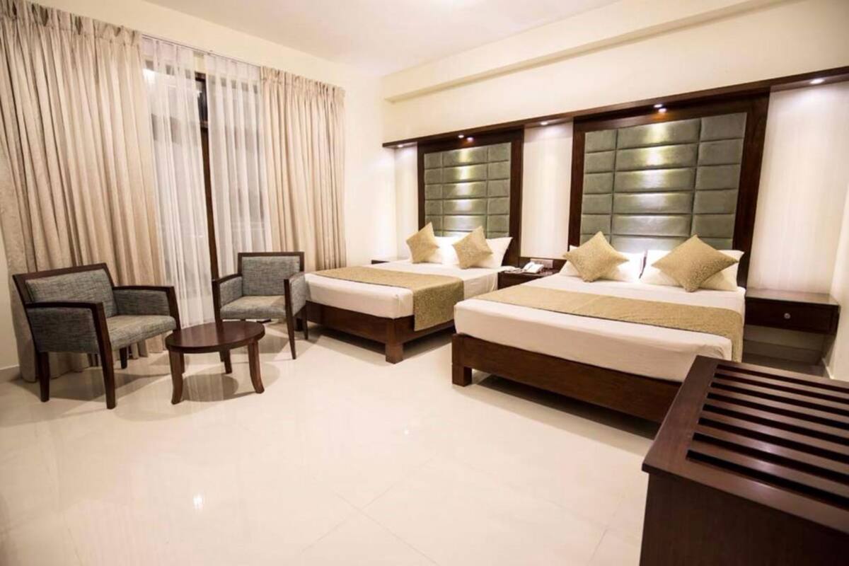 Quarto de hotel com duas camas, um sofá, uma poltrona e uma mesa pequena.