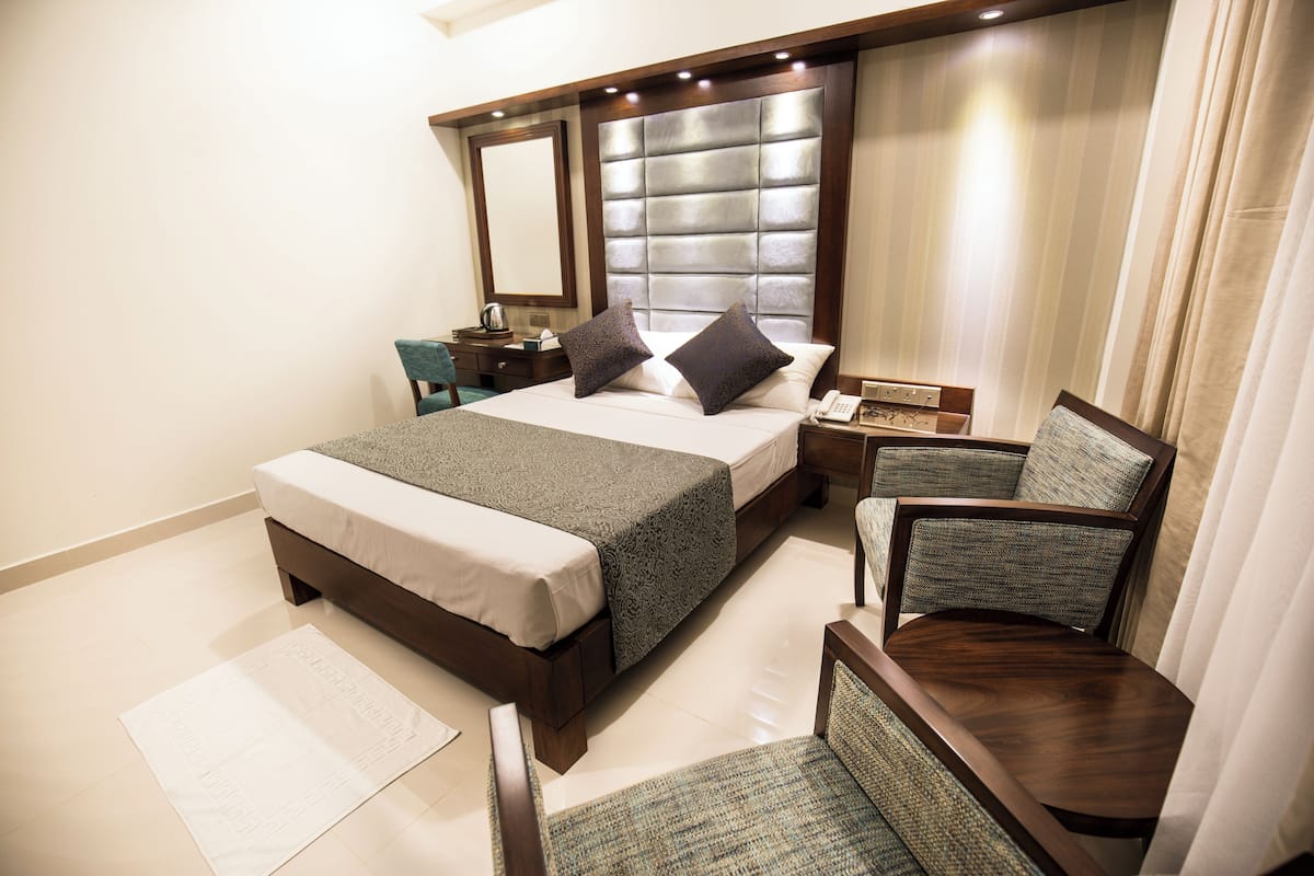 Quarto de hotel com uma cama grande, uma mesinha de cabeceira, uma cadeira e um espelho.