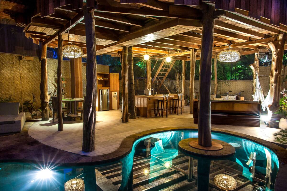 Uma área de piscina com deck de madeira, espreguiçadeiras e um bar.