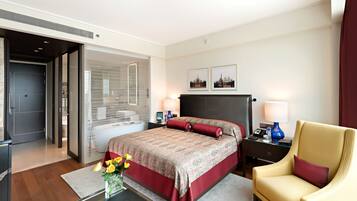Quarto de hotel moderno com cama grande, mesas de cabeceira, uma cadeira e vista para a cidade pela janela.