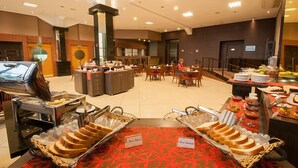 Uma área de buffet com diversos alimentos e uma mulher servindo.