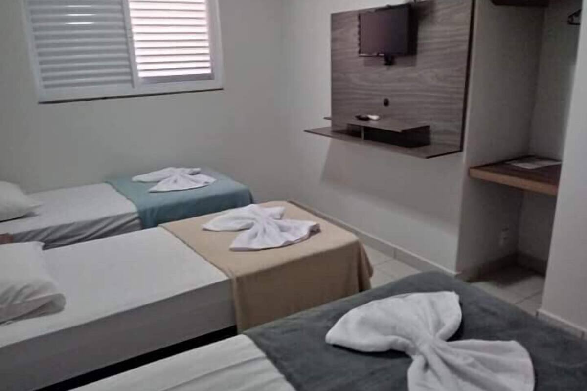 Quarto de hotel com duas camas, uma pequena mesa, televisão e janela com persianas.