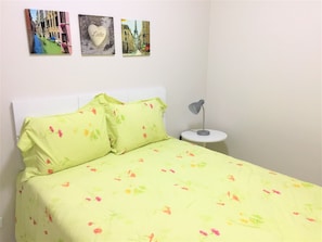 Uma cama com roupa de cama florida, um abajur e três quadros na parede.