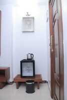 Um quarto pequeno com um banco de madeira, uma lixeira, um quadro na parede e uma porta com puxador.