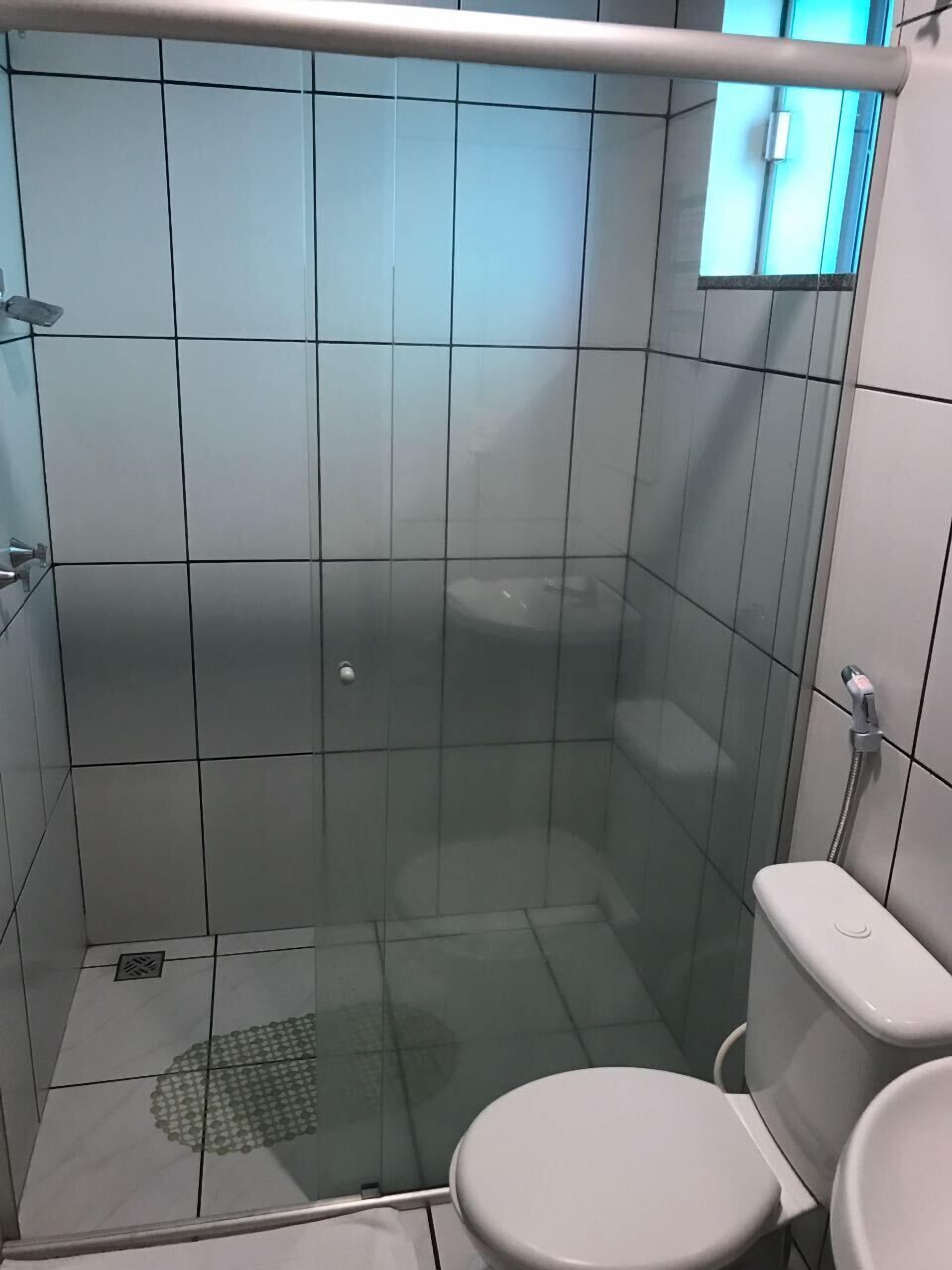 Um espaço de chuveiro pequeno e fechado, com porta de vidro, vaso sanitário e ralo aparente.