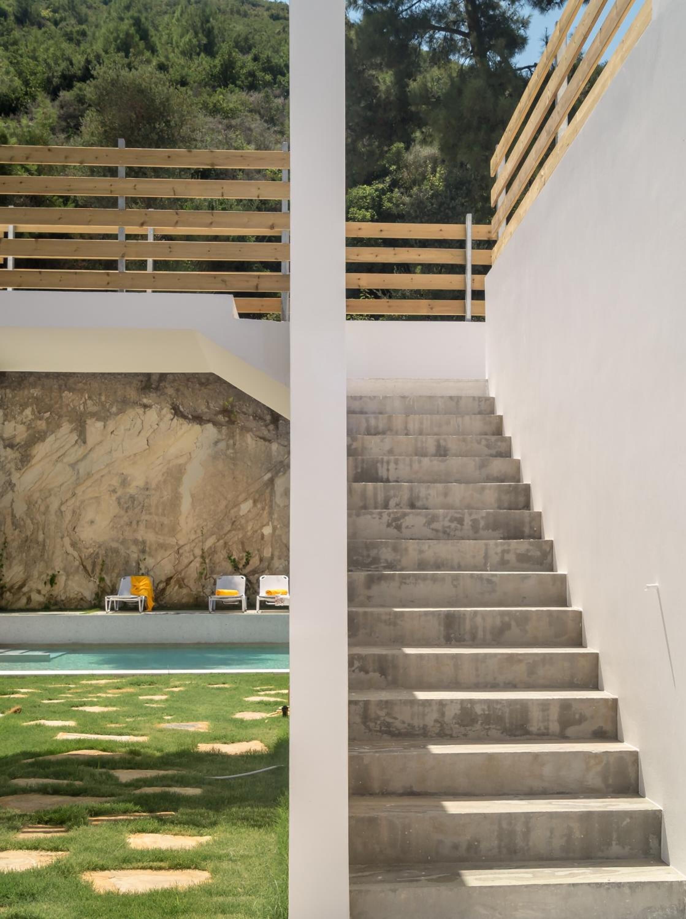 Uma área de piscina moderna ao ar livre, com uma parede de pedra, um deck de madeira e uma escadaria de concreto.