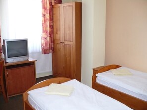 Quarto com duas camas de madeira, um guarda-roupa de madeira, uma escrivaninha com um laptop e uma janela com cortinas.