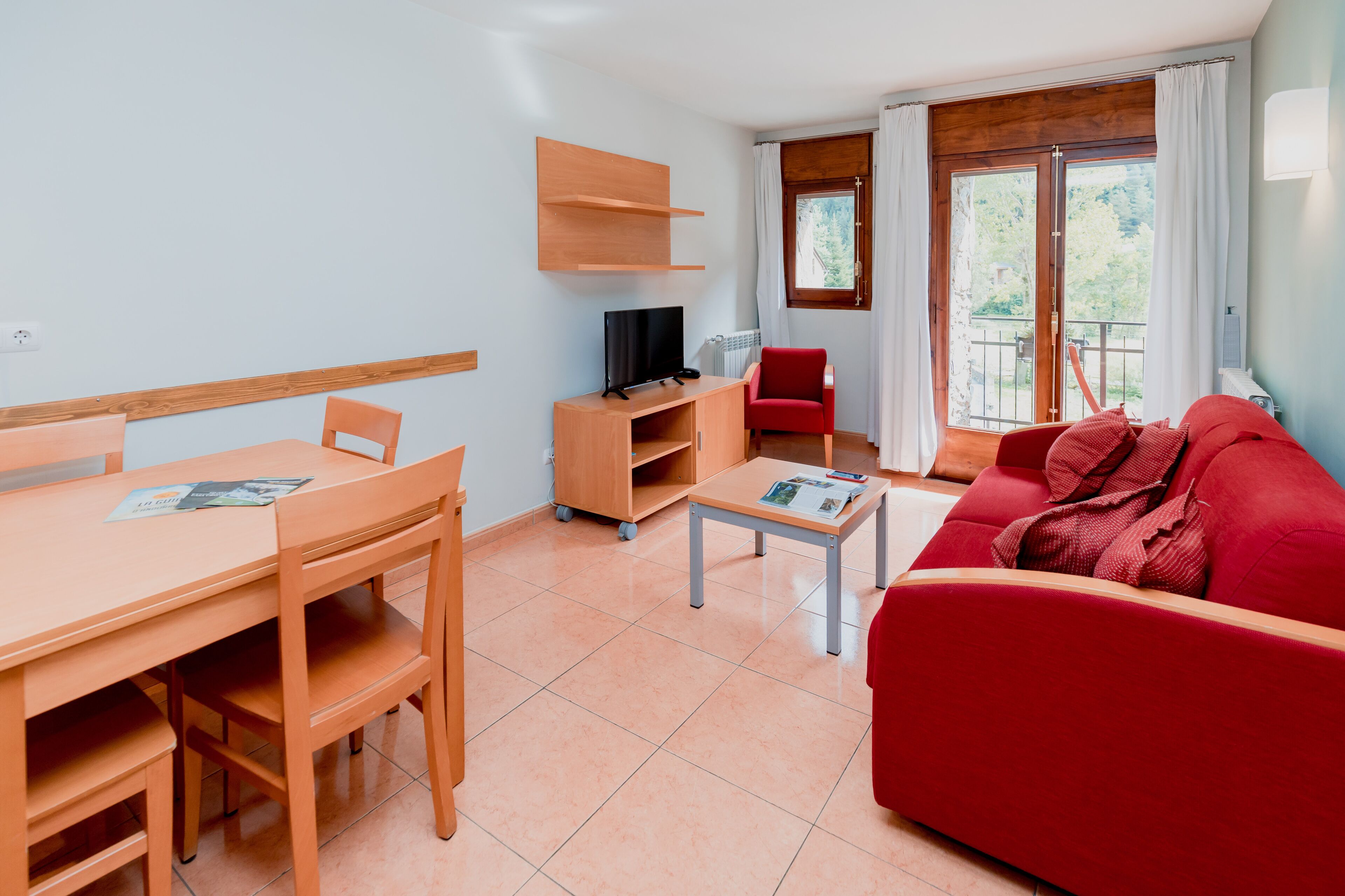Uma sala de estar moderna com um sofá vermelho, mesa de jantar de madeira e uma TV sobre um suporte de madeira.