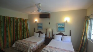 Quarto de hotel com duas camas, ventoinha no teto, ar condicionado fixado na parede e duas luminárias fixadas na parede.